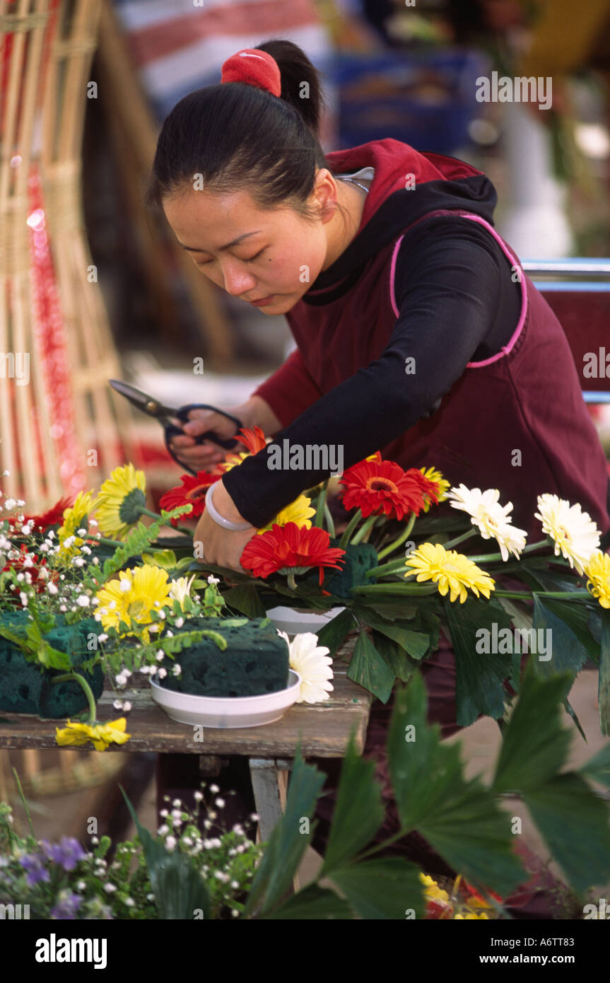China, Yunnan, Kunming. Woman arranges flowers at city flower market ...
