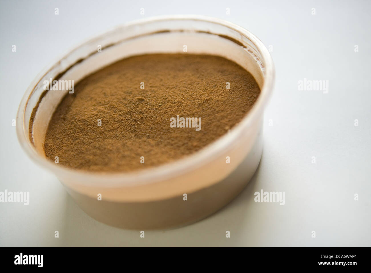 Studio shot of an open plastic container of cinnamon powder on a plain ...