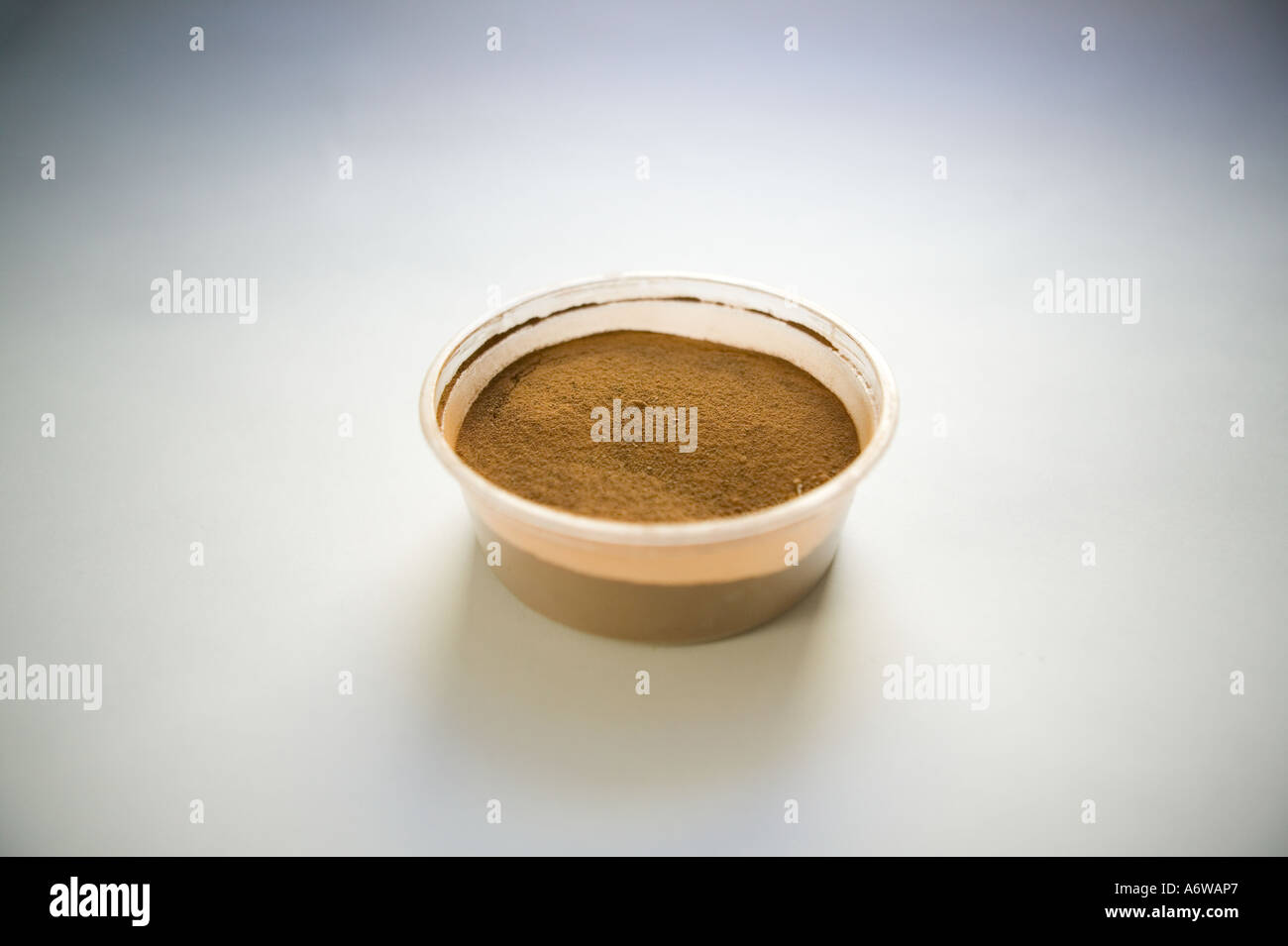Studio shot of an open plastic container of cinnamon powder on a plain ...