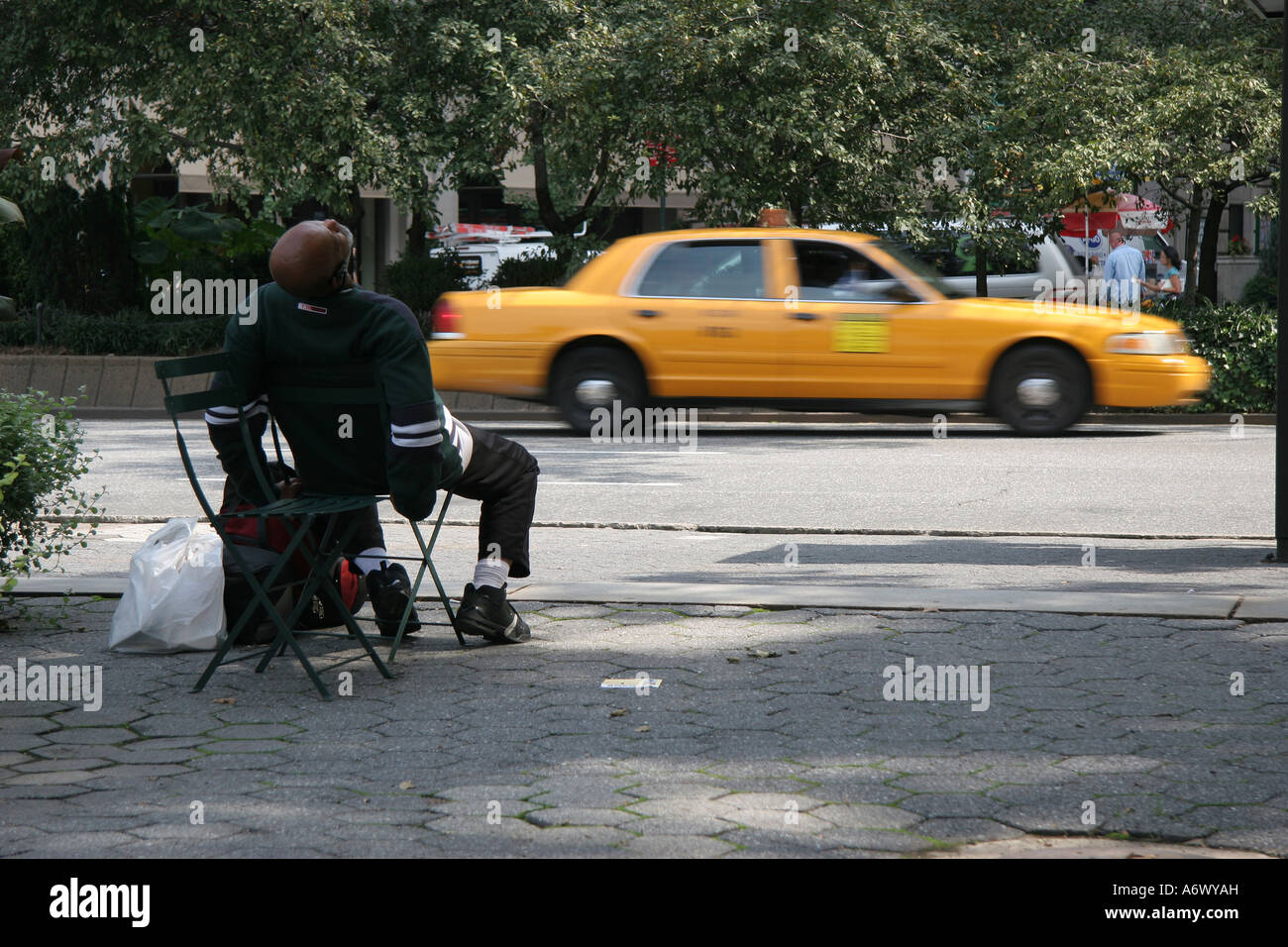 Rear view of a man sitting at the roadside with a taxi moving on the ...