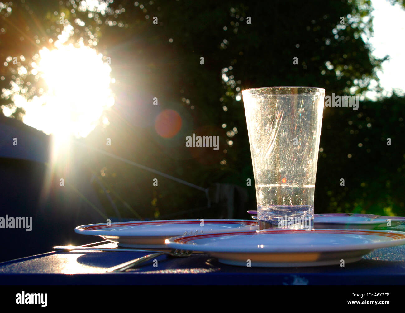 Picnic table with plates and glass lit by setting sun Stock Photo - Alamy