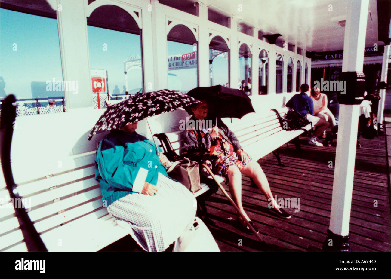 Two ladies sitting in the shade on Brighton pier under umbrellas UK ...