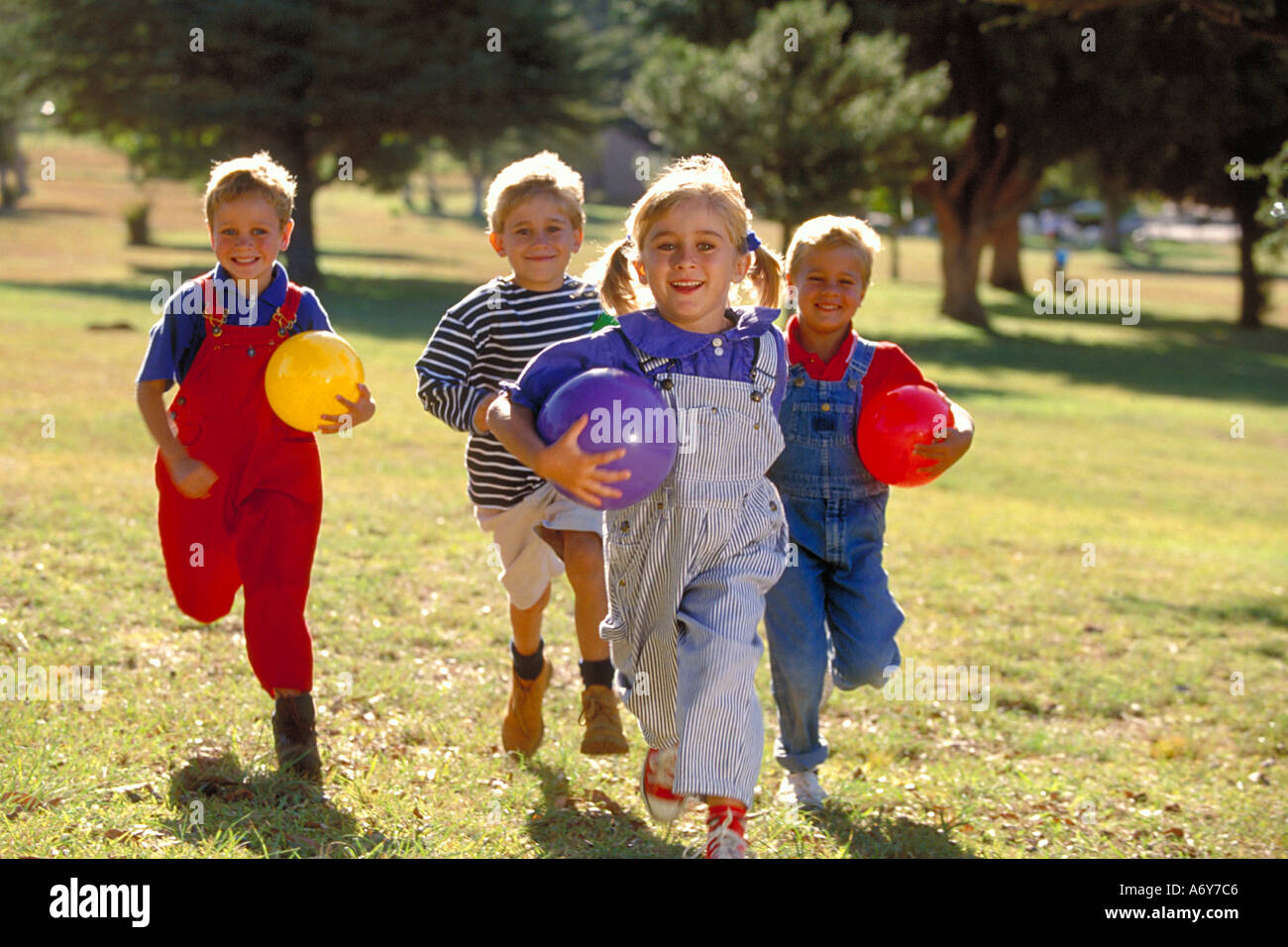 portrait of a group of kids running on a meadow with plastic balls ...