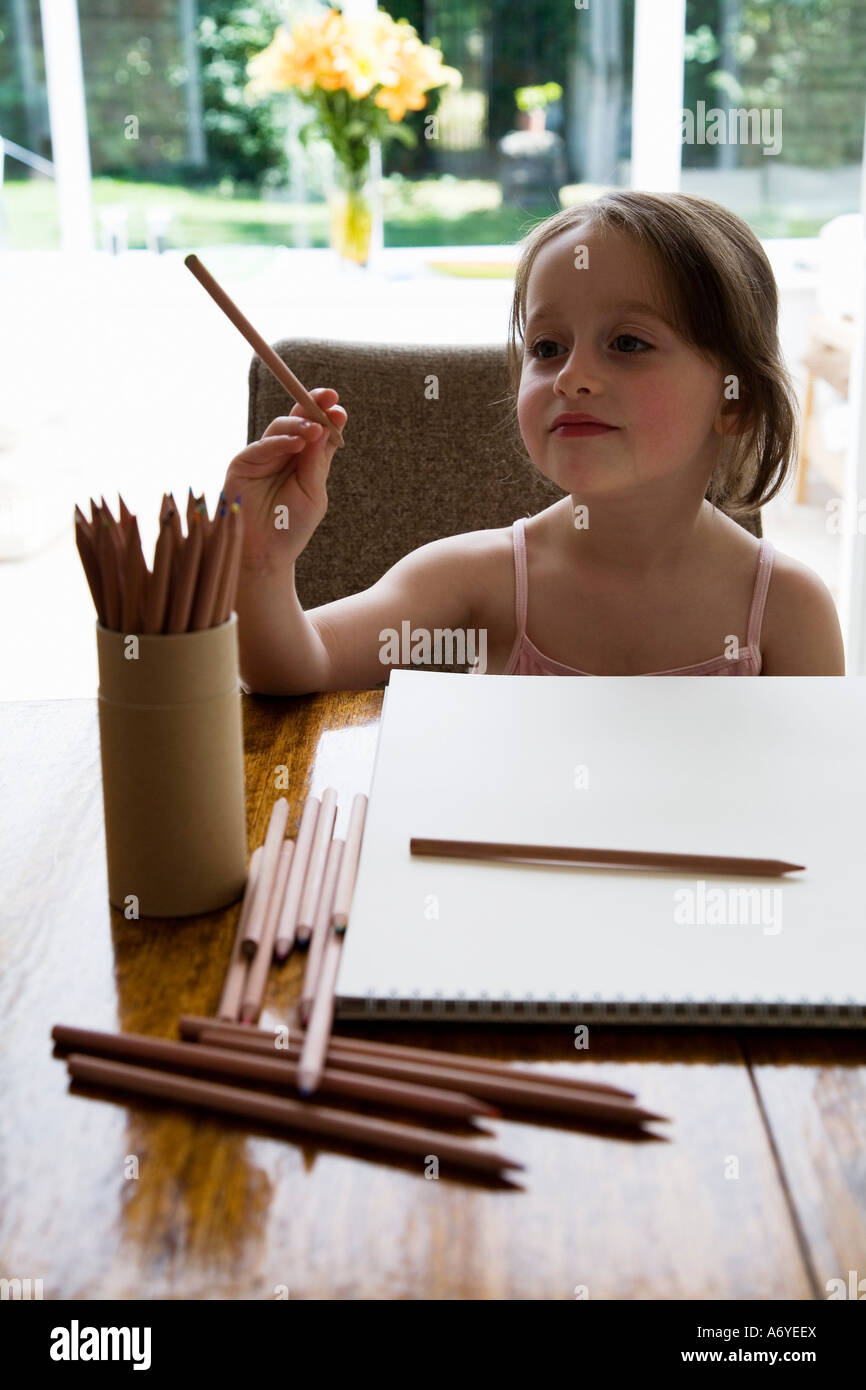 Young girl sitting at a table with a sketch pad and colored pencils ...