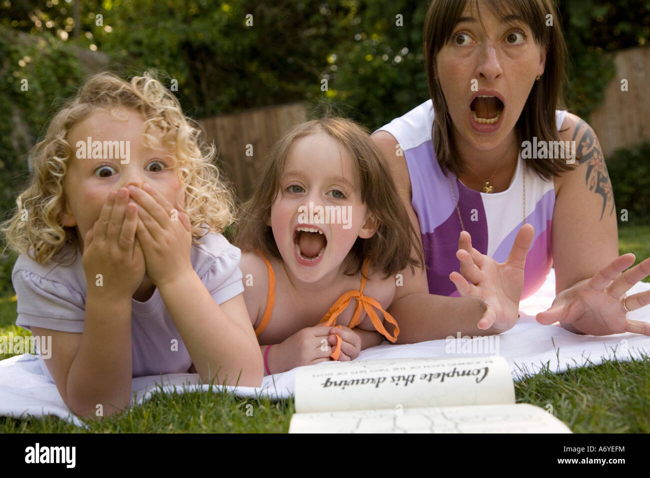 A woman and two girls screaming whilst lying down in a backyard Stock ...