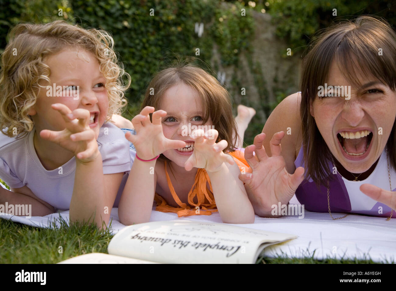 A woman and two girls growling whilst lying down in a backyard Stock ...