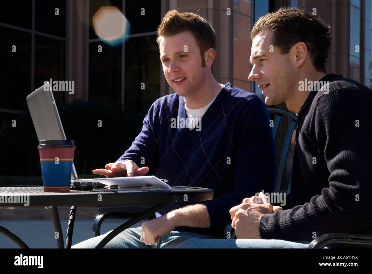 Two men looking at a laptop computer at an outdoor cafe Stock Photo - Alamy