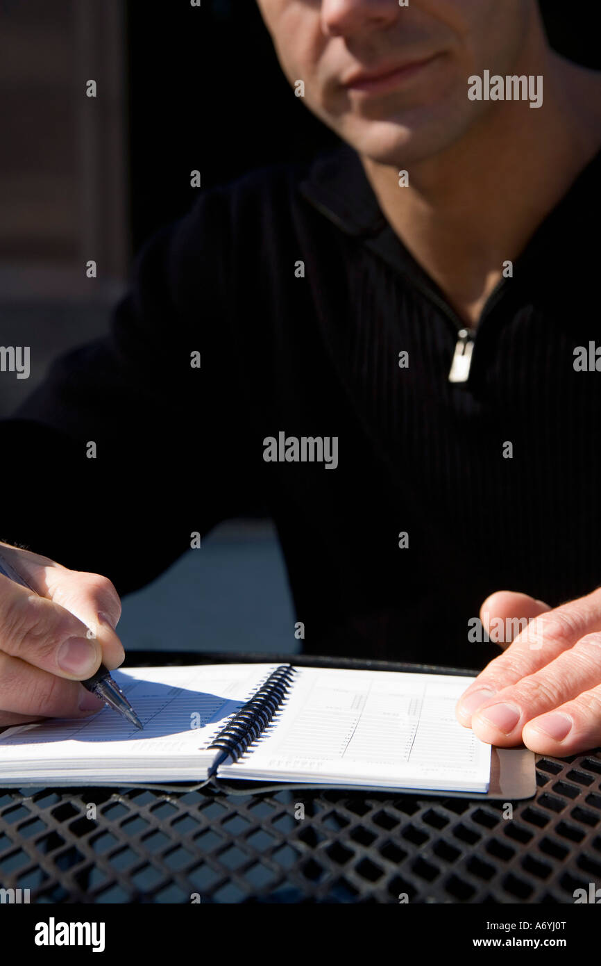 Man sitting outdoors at a table and writing in a personal organizer ...