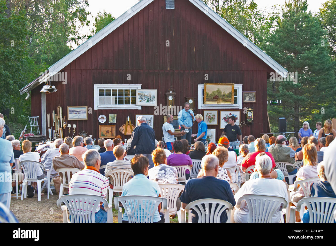 A country side auction with buyers sitting in white plastic chairs ...