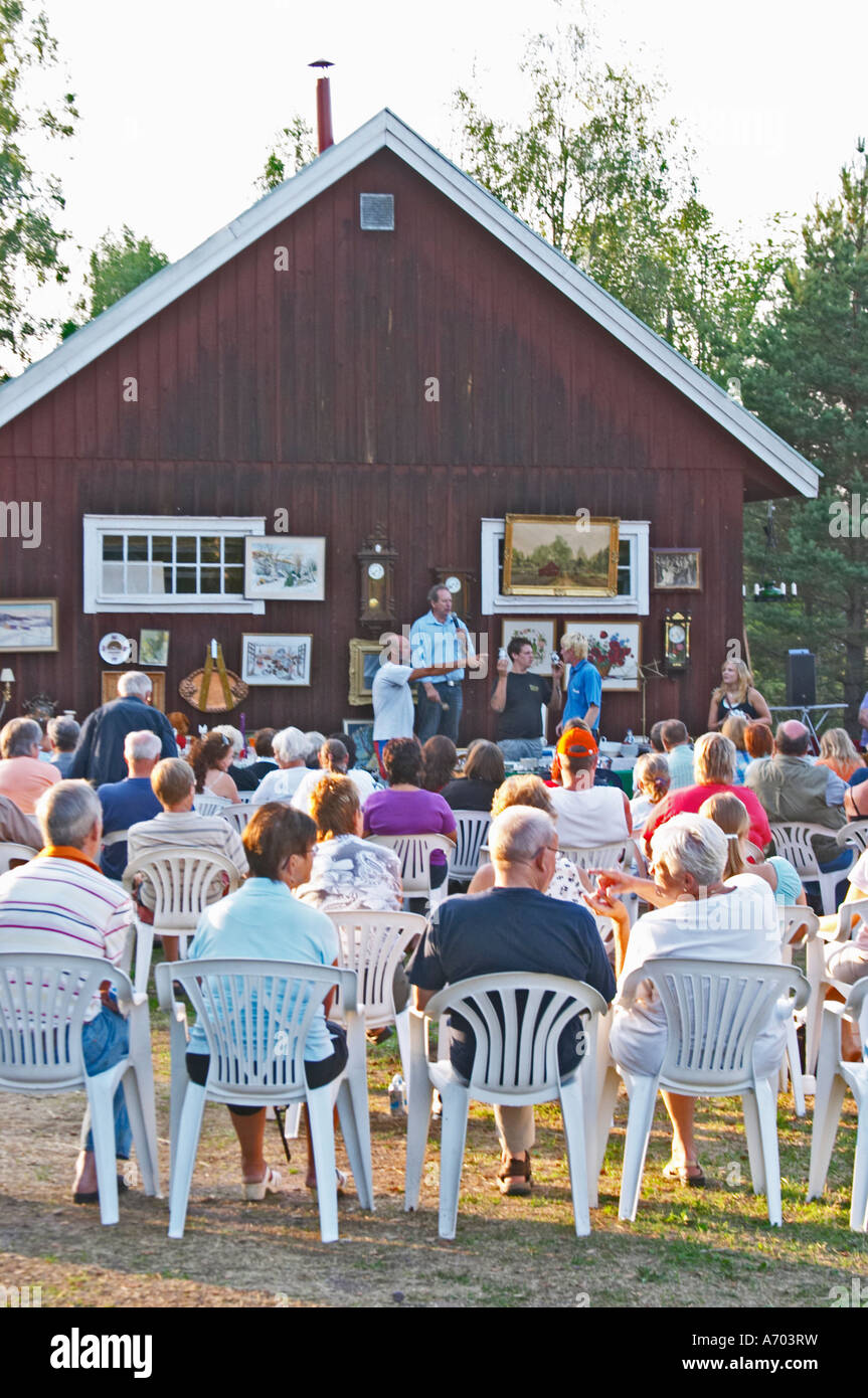 A country side auction with buyers sitting in white plastic chairs ...