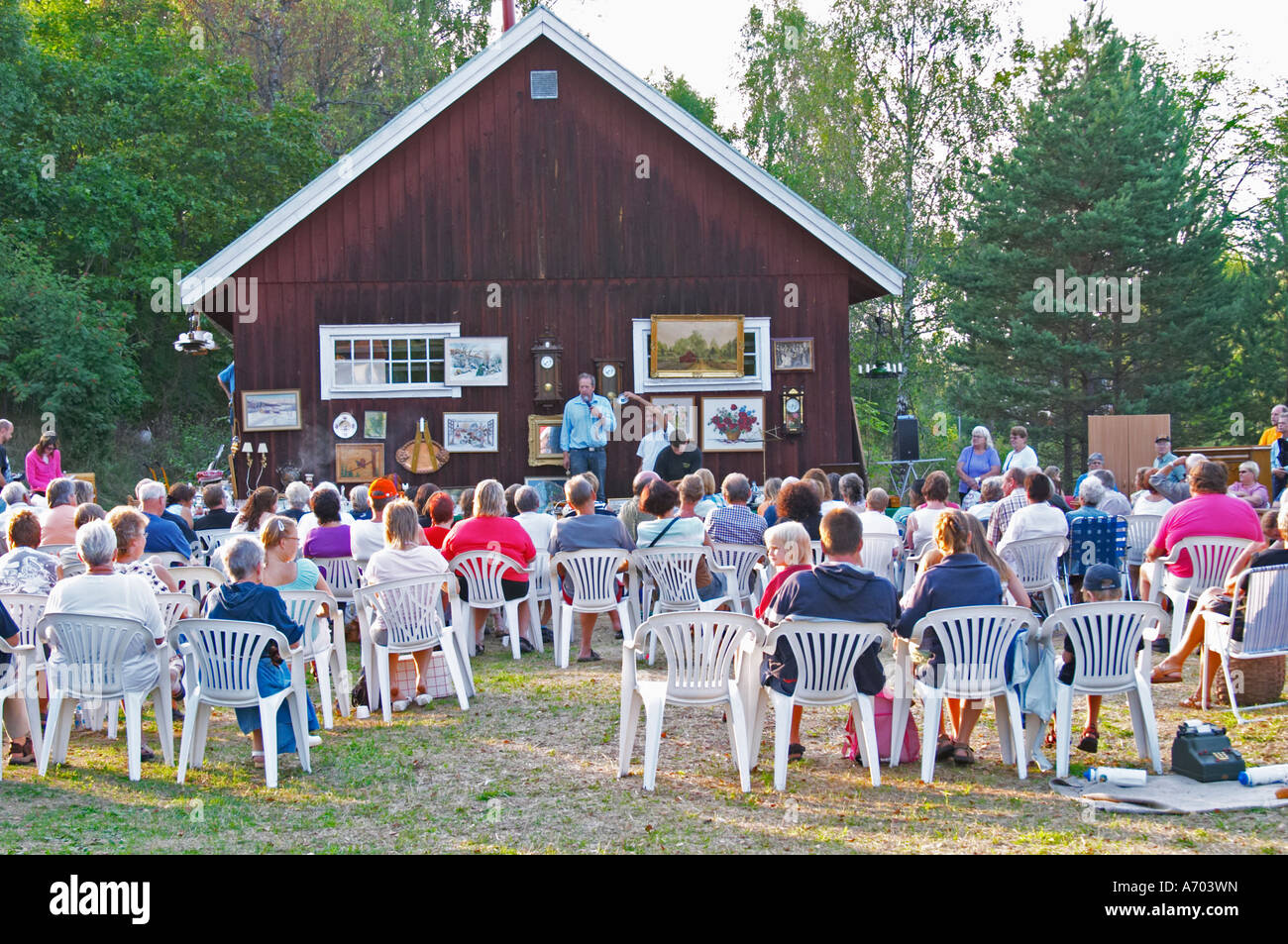 A country side auction with buyers sitting in white plastic chairs ...