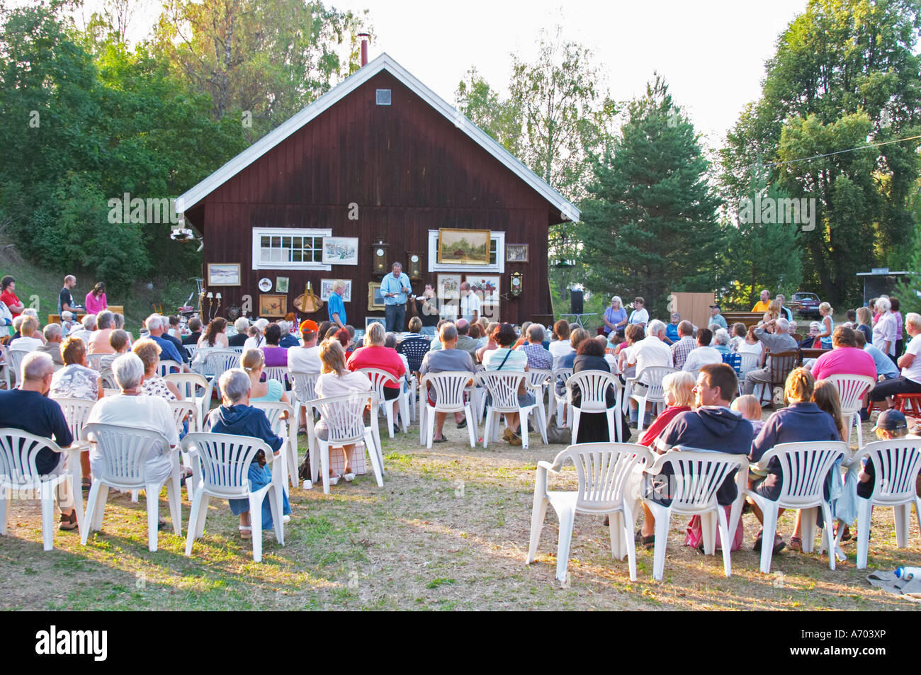 A country side auction with buyers sitting in white plastic chairs ...