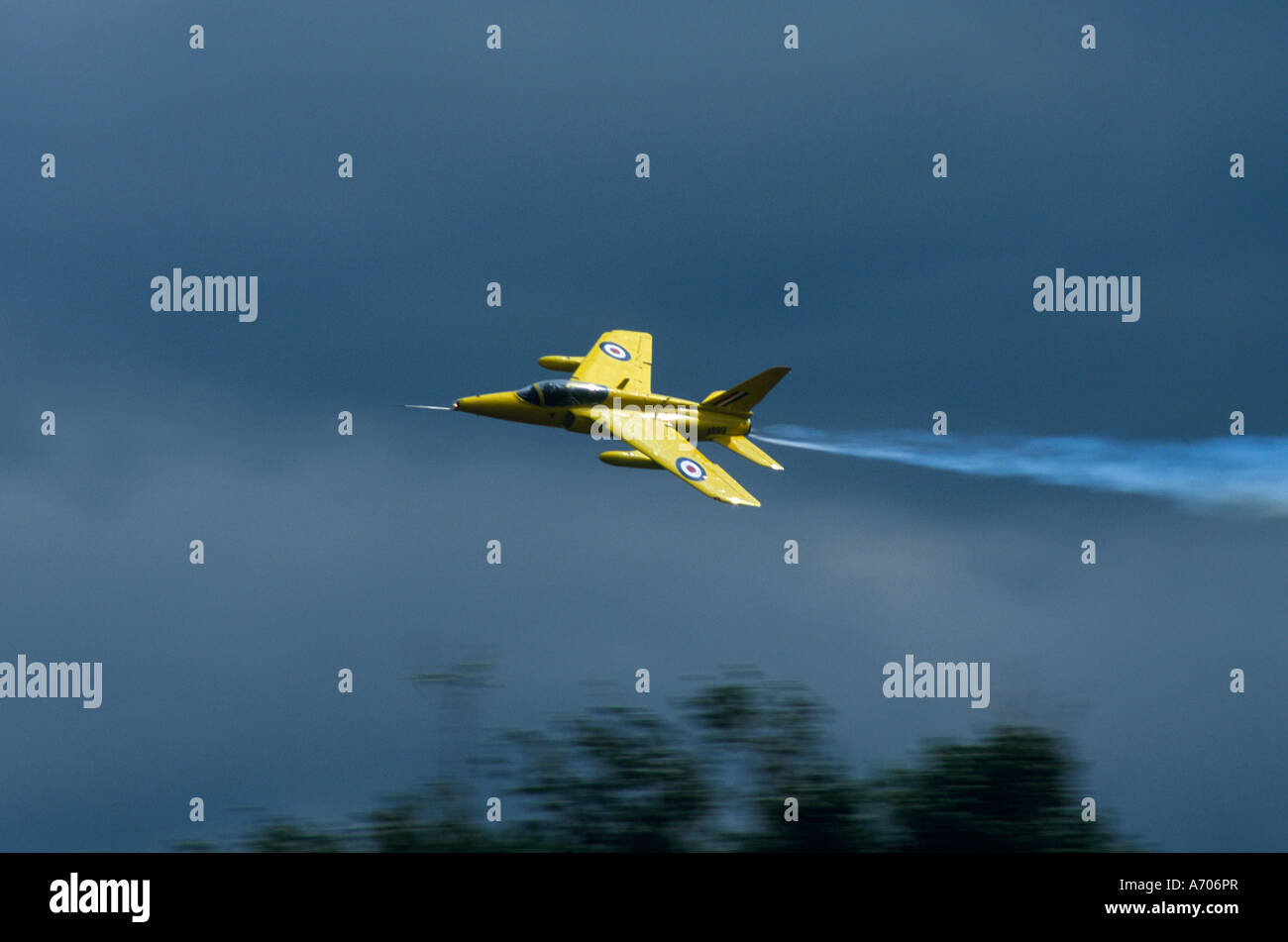 Yellow Hawker Hawk jet trainer aircraft flying against dark grey clouds ...