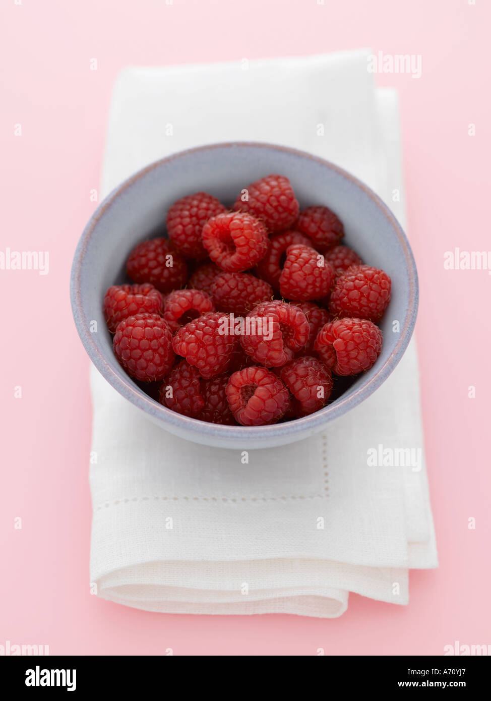 Raspberries in ceramic bowl with white linen napkin on pale pink ...