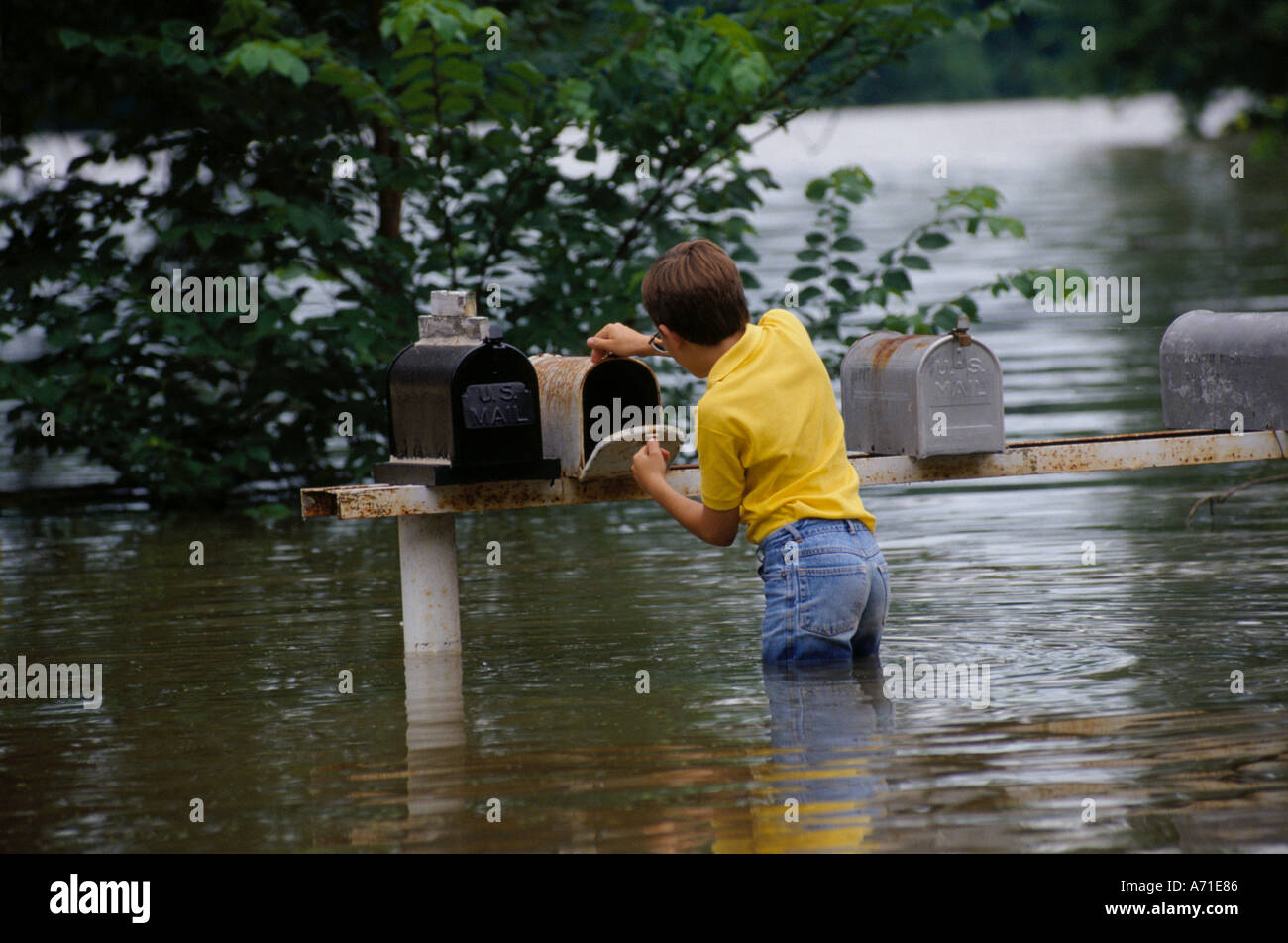 Boy geting mail out of mailbox in waist deep water after rains have ...