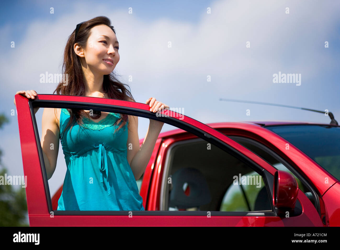 Young woman leaning against open door of car Stock Photo - Alamy