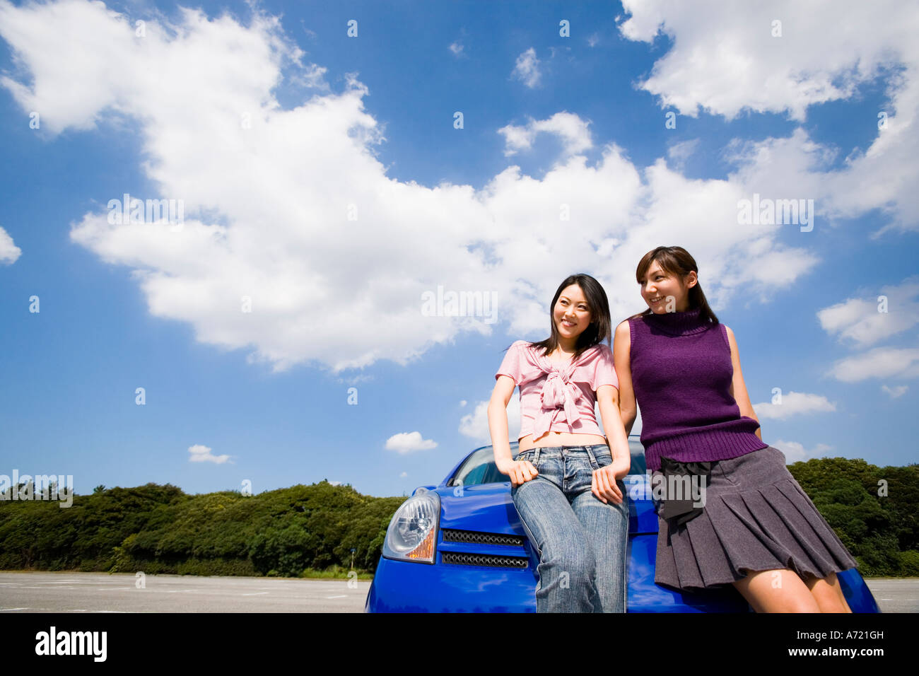 Two young women leaning against car Stock Photo - Alamy
