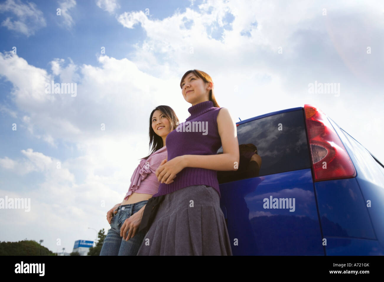 Two young women leaning against car Stock Photo - Alamy