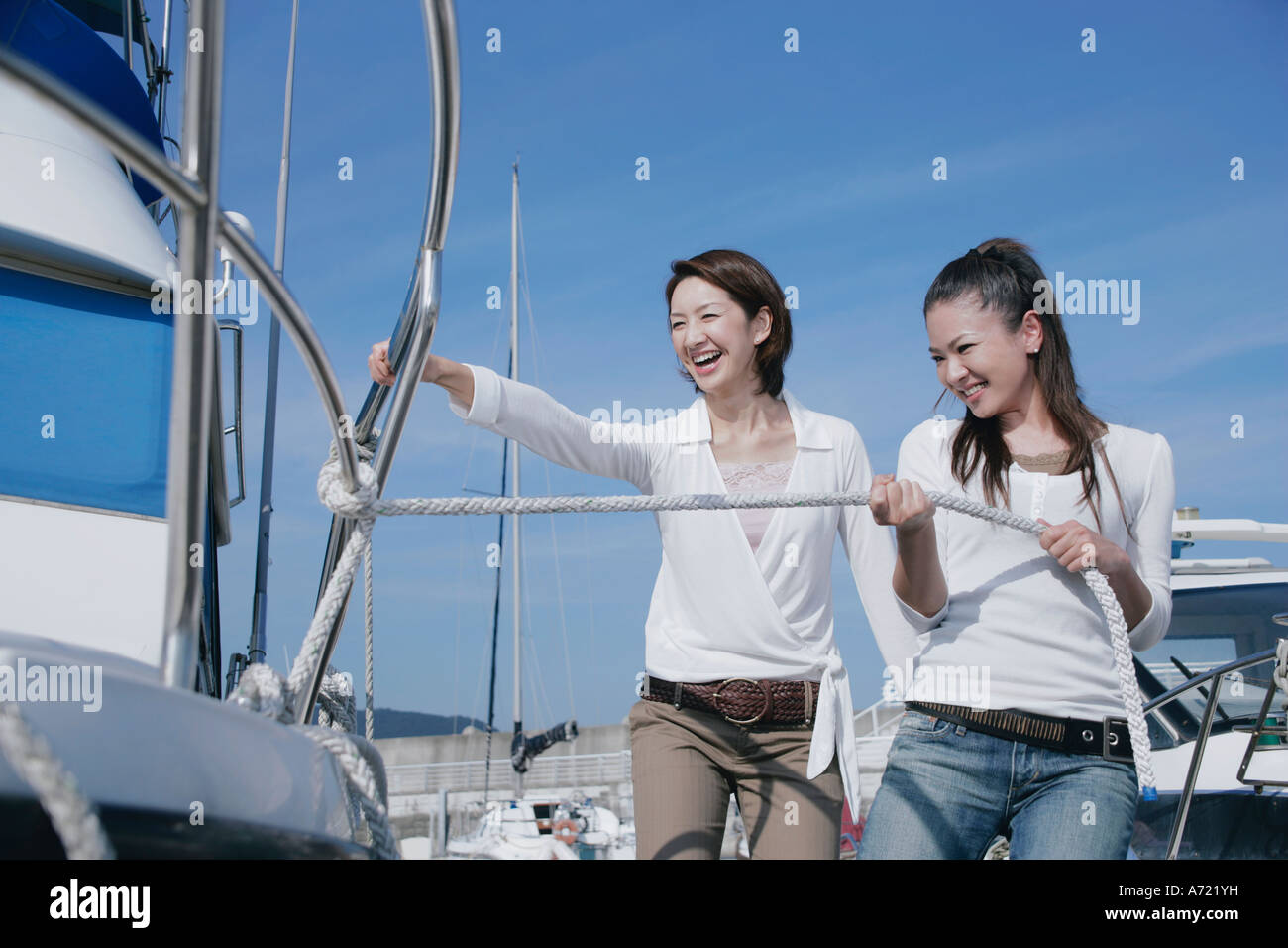 Two young women pulling rope attached to yacht Stock Photo - Alamy