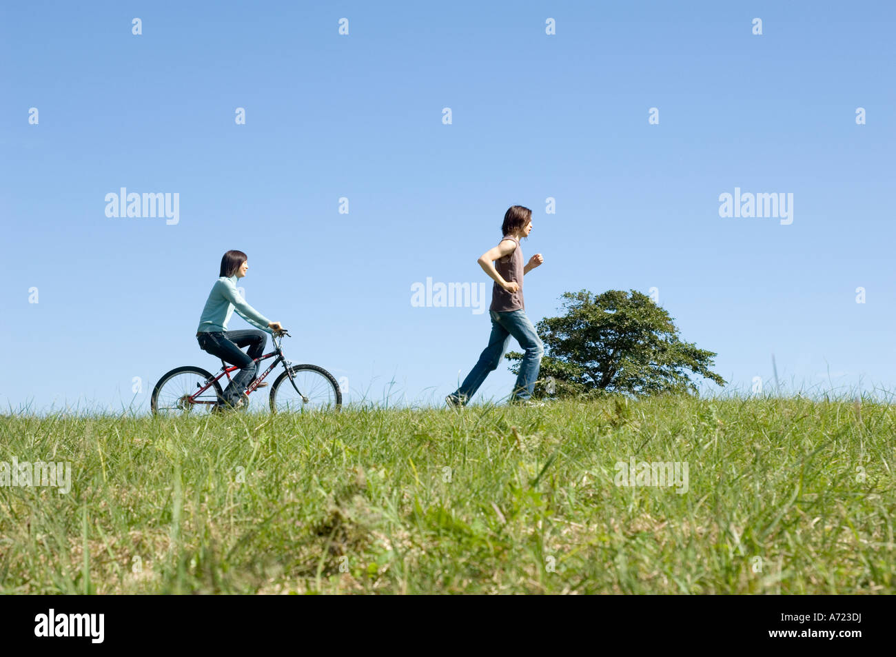 Young woman riding bicycle behind young man running Stock Photo - Alamy