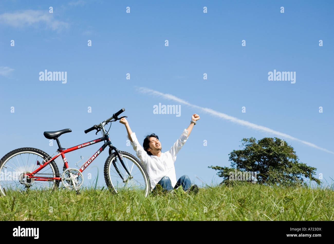 Young man sitting next to bicycle, arms outstretched Stock Photo - Alamy