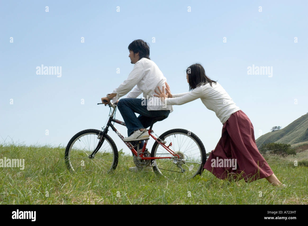 Young woman pushing young man on bicycle Stock Photo - Alamy