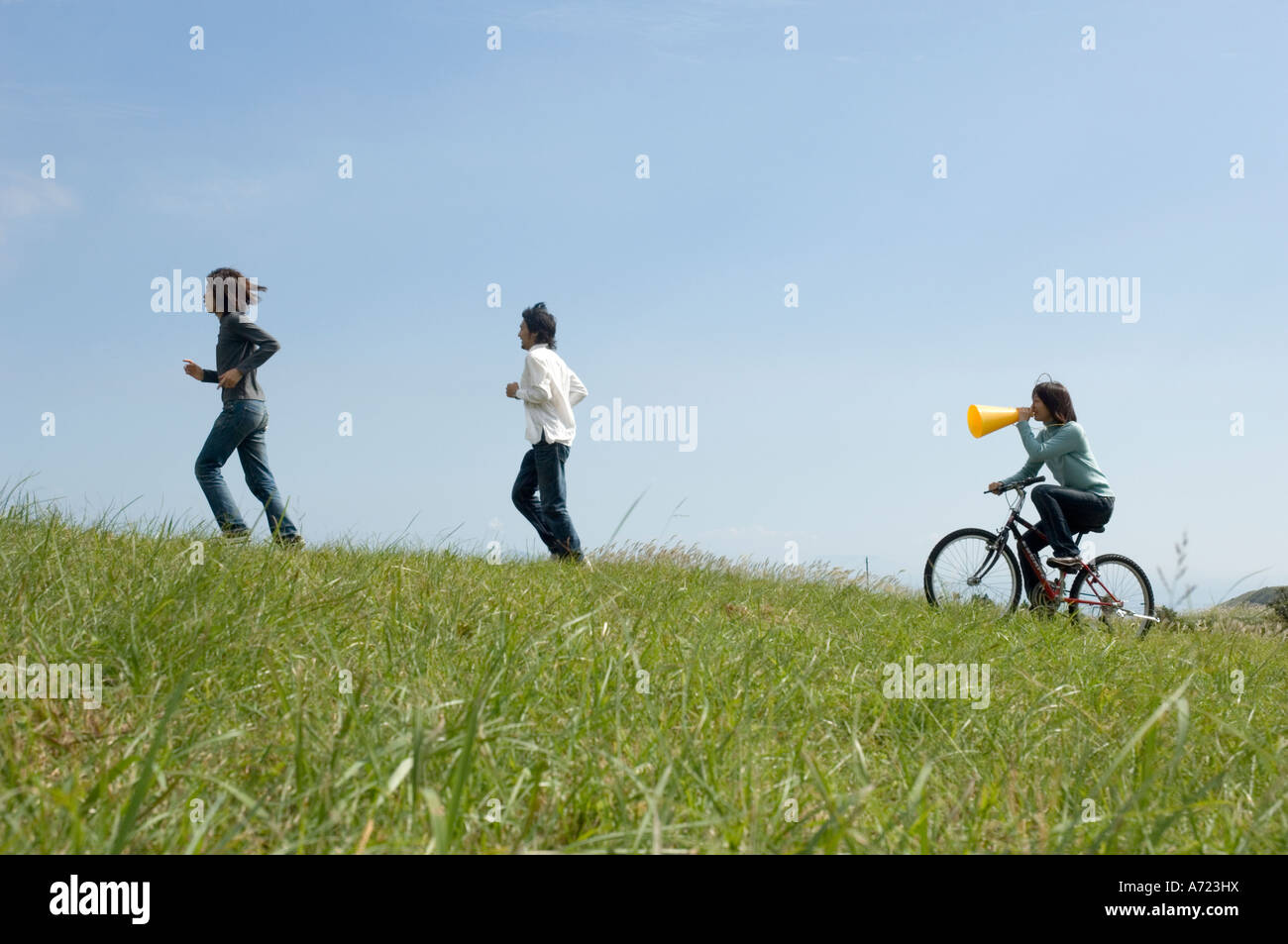 Young woman riding bicycle behind two young men running Stock Photo - Alamy