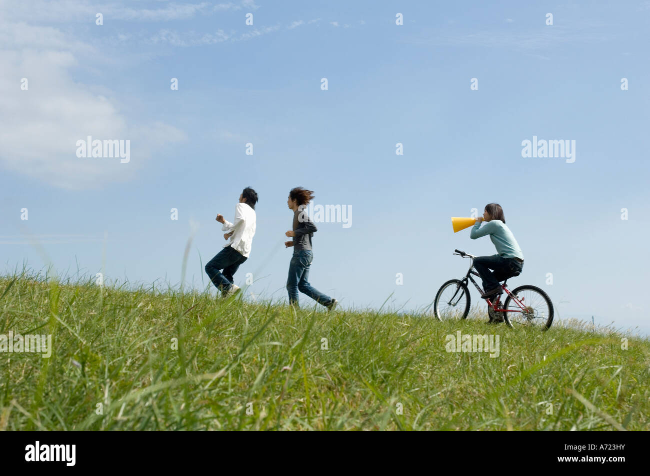 Young woman riding bicycle behind two young men running Stock Photo - Alamy