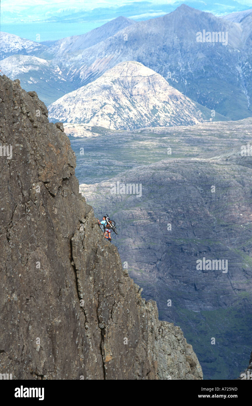 Man with mountain bike on his back climbing very steep ridge Cuillin ...