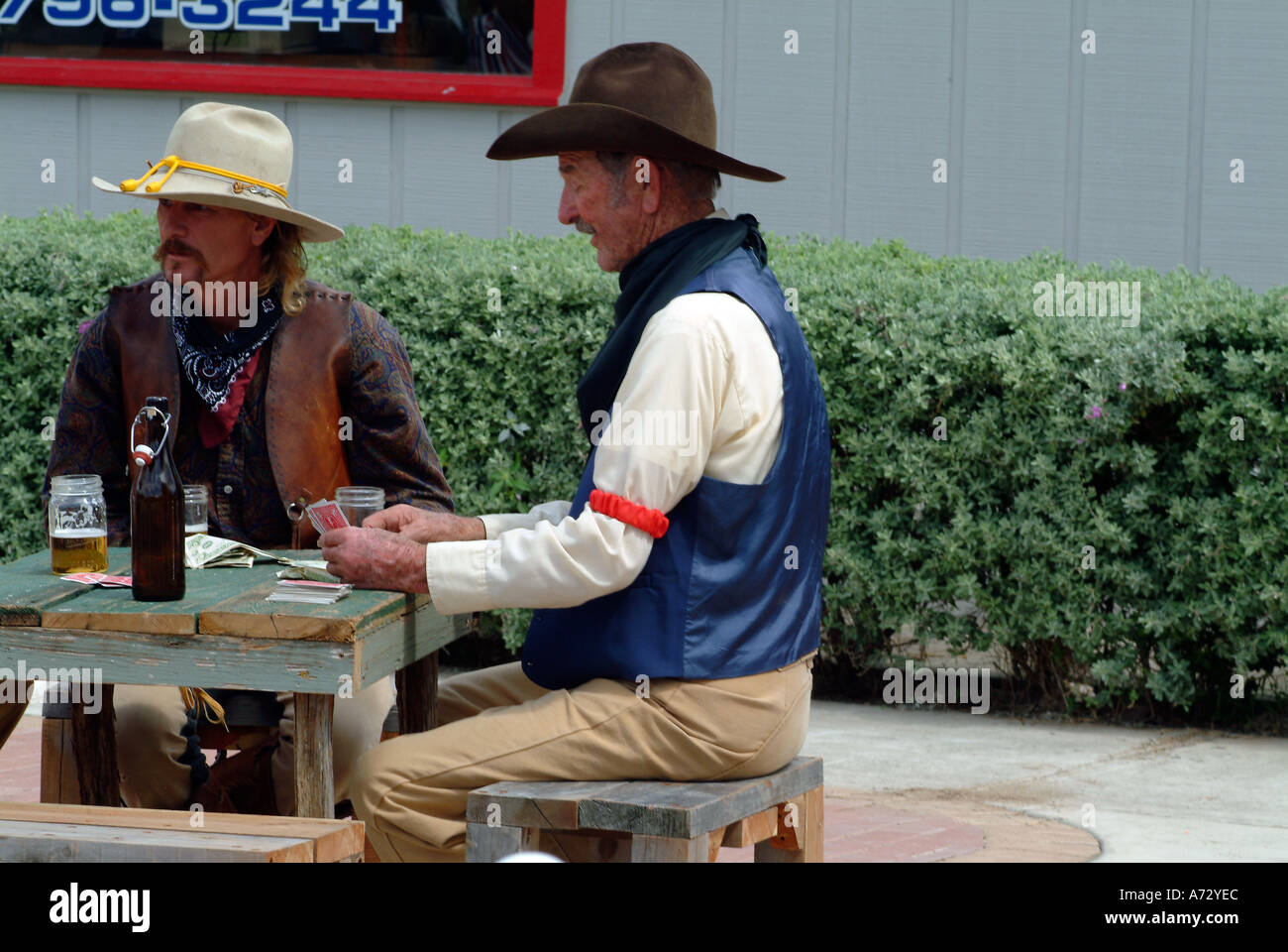 Actors acting cowboys playing cards sitting around a wood table Stock ...