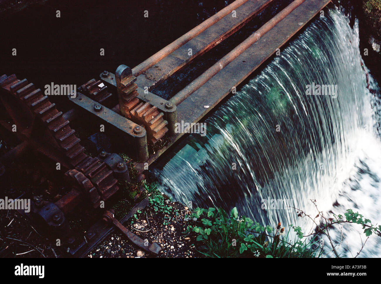 Water going over a small weir with rusty gear wheels Stock Photo - Alamy