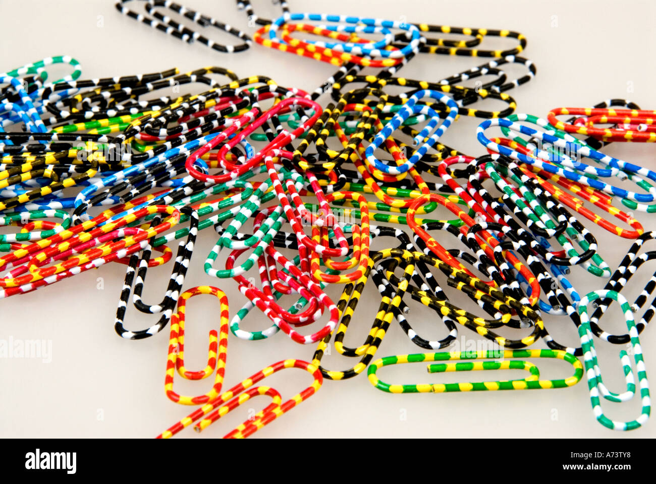 A pile of multicoloured striped paperclips against a white background ...