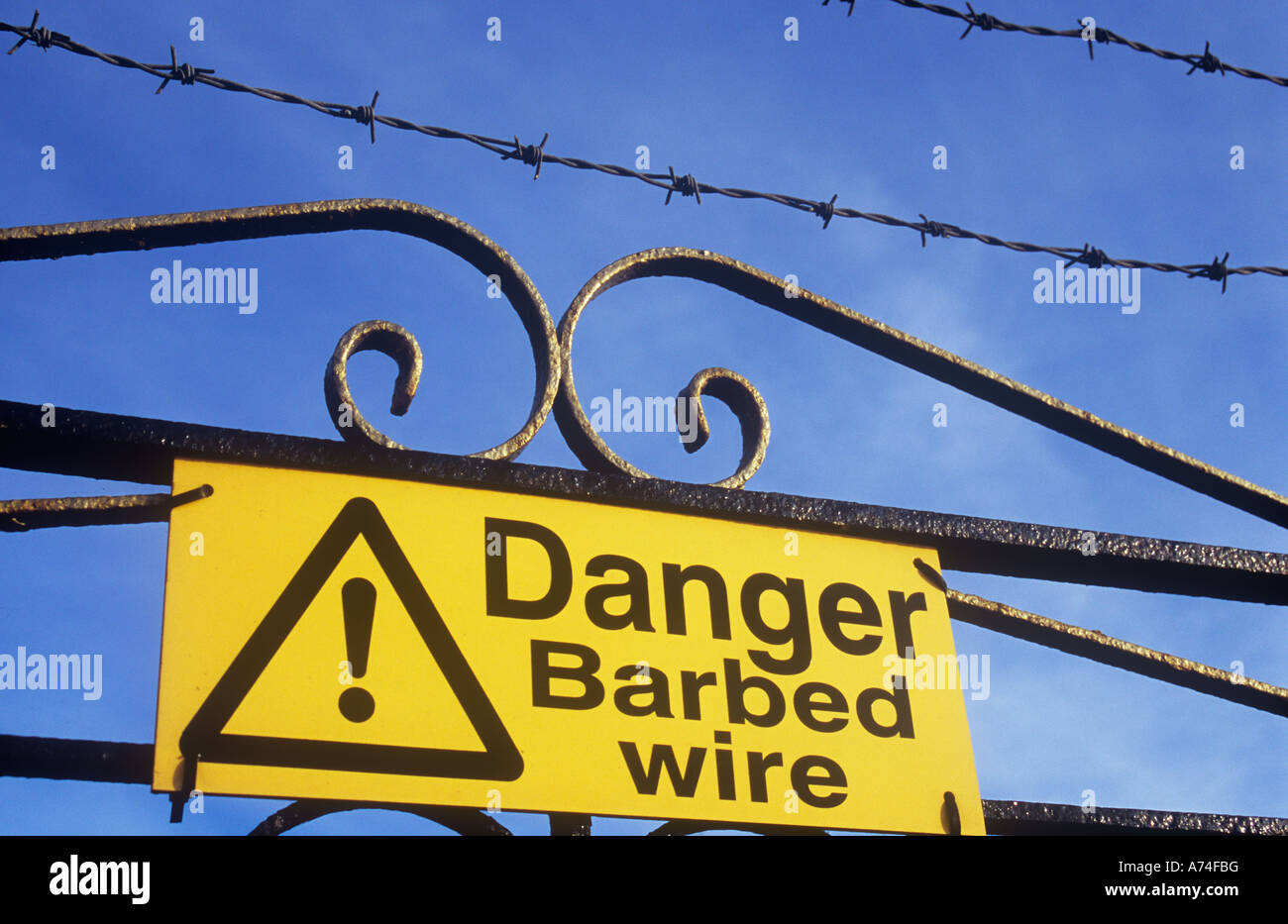 Yellow and black sign with warning triangle stating Danger Barbed wire ...