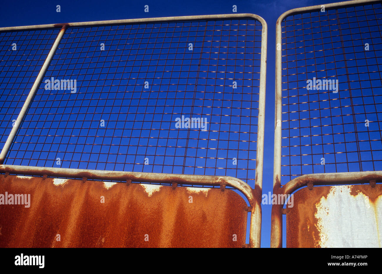 Detail of rusting aluminium gates topped with wire mesh with deep blue ...