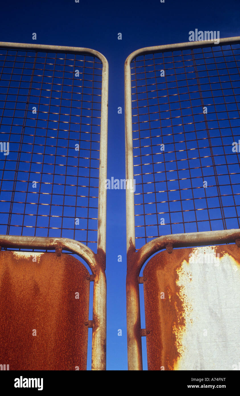 Detail of rusting aluminium gates topped with wire mesh with deep blue ...
