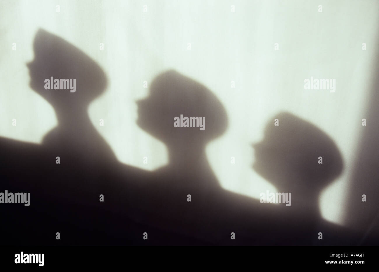 Shadow in warm light on pale cloth or curtain of three model adult ...