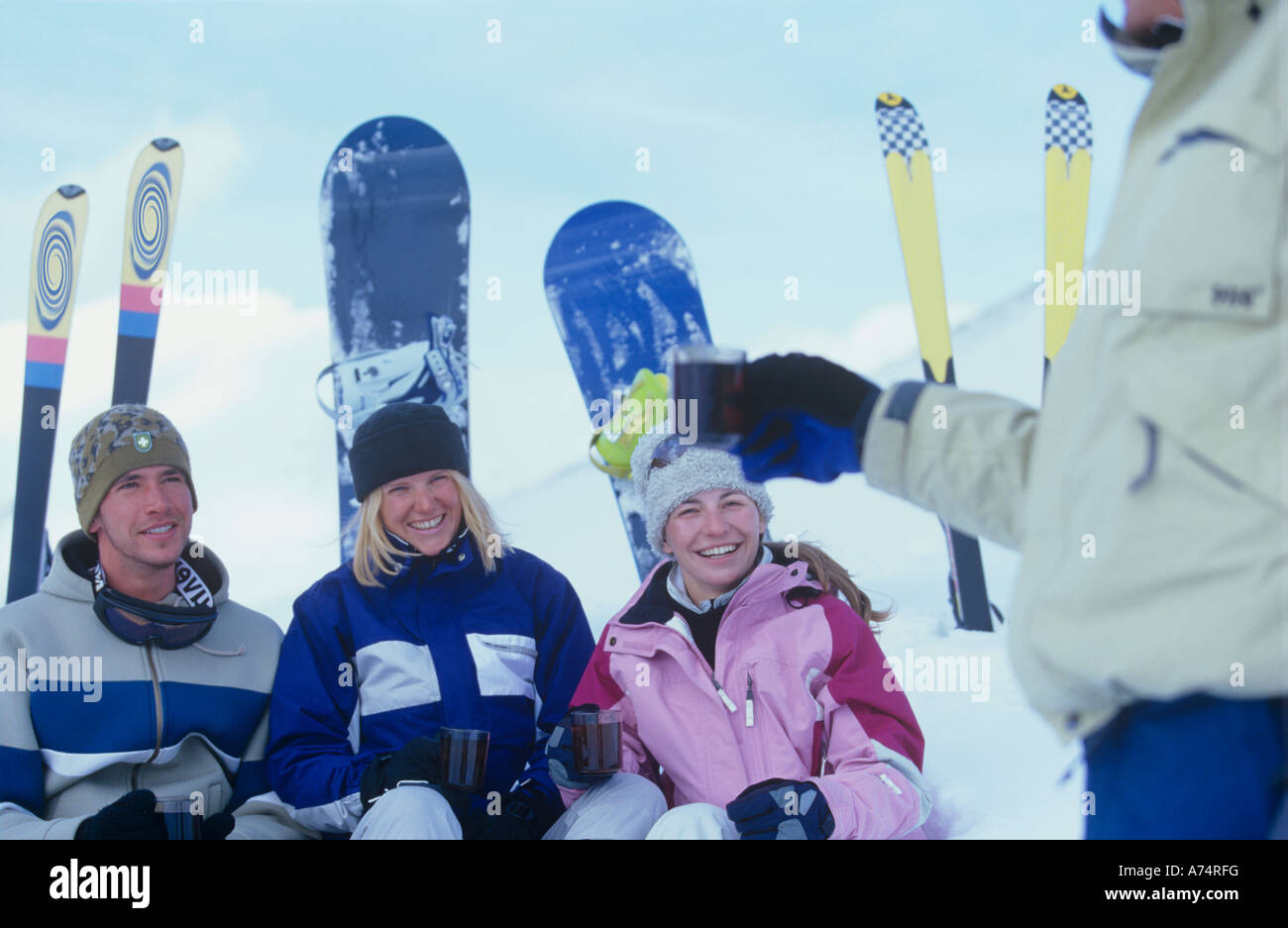 group of four friends sitting in snow drinking mulled wine Stock Photo ...
