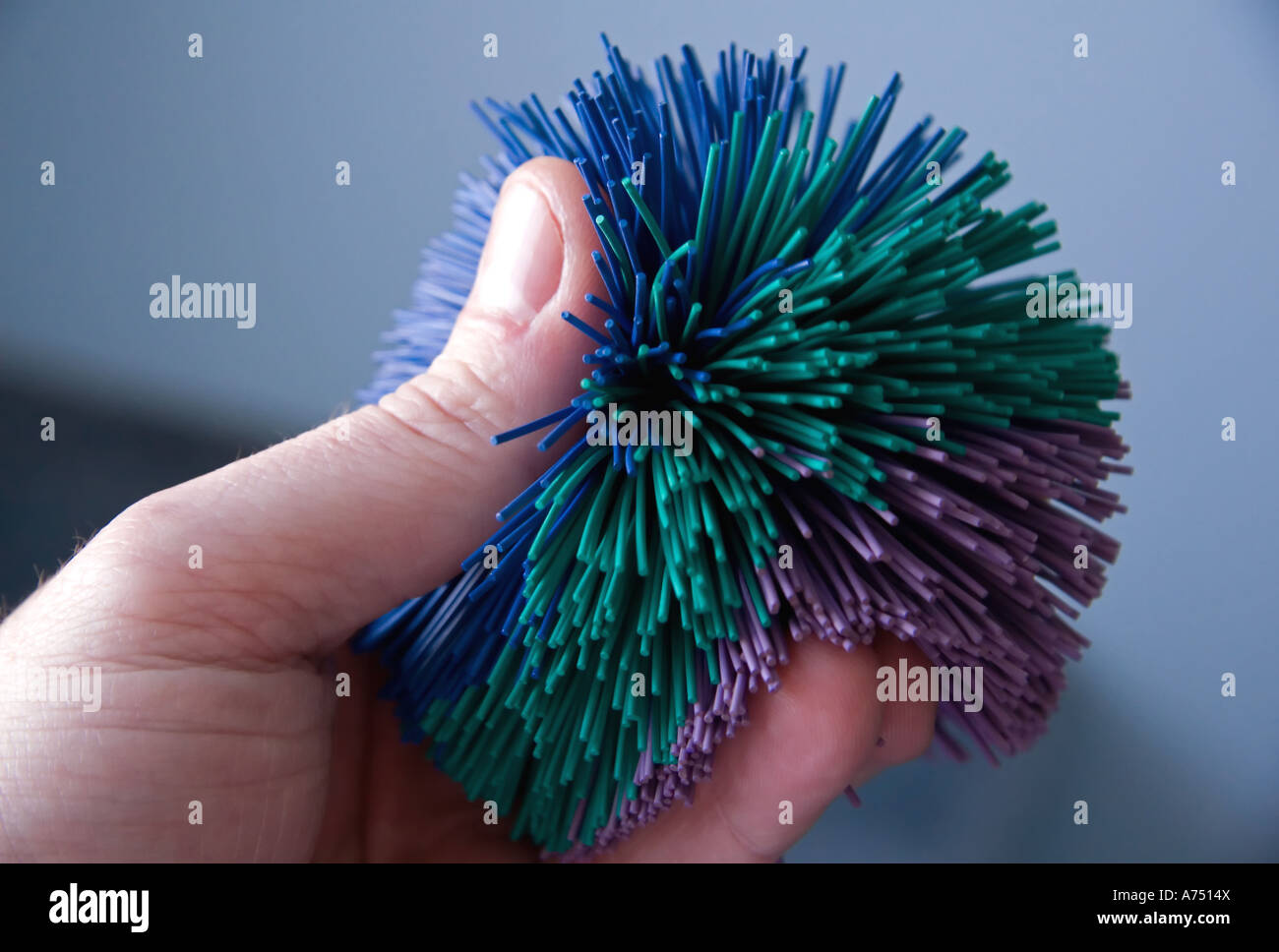 A hand squeezing a "koosh" ball toy. The colorful, rubbery fingers are ...