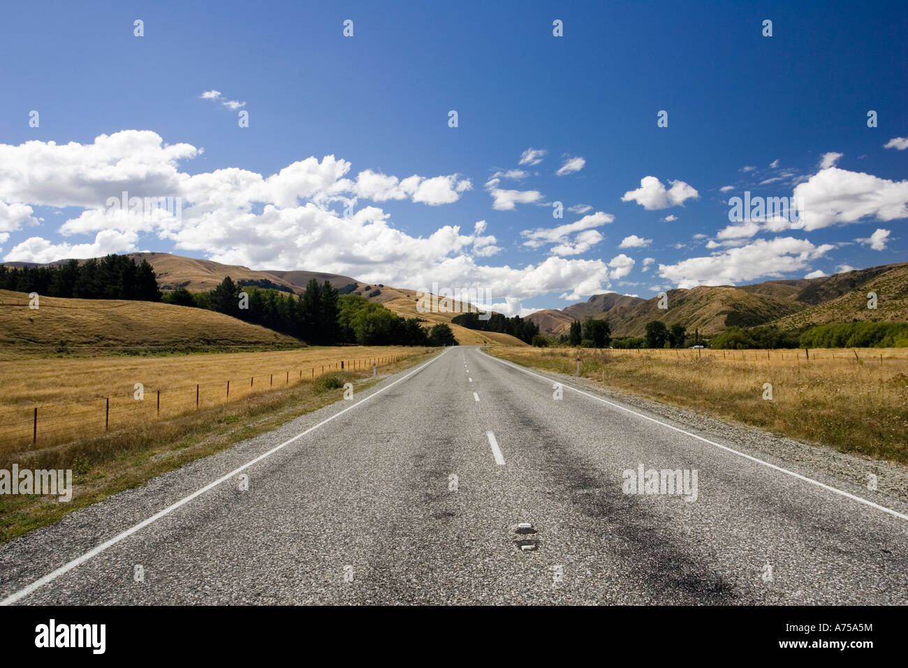 Long straight deserted tarmac paved road rolling hills white clouds ...