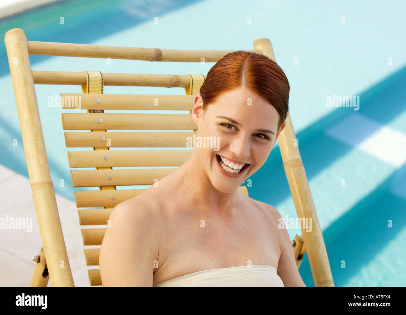 Woman sitting in deckchair smiling, pool in background Stock Photo - Alamy