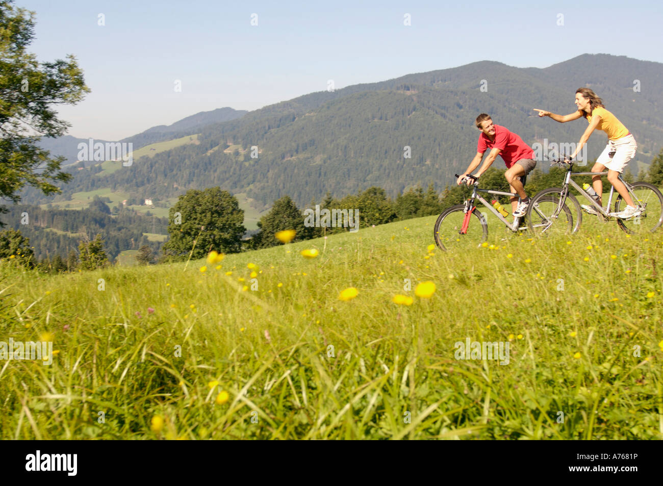 Young couple riding mountain bike in meadow, side view, mountains in ...