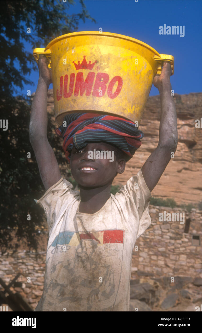A Dogon boy carrying a JUMBO bucket of water on his head, Tereli, Pays ...