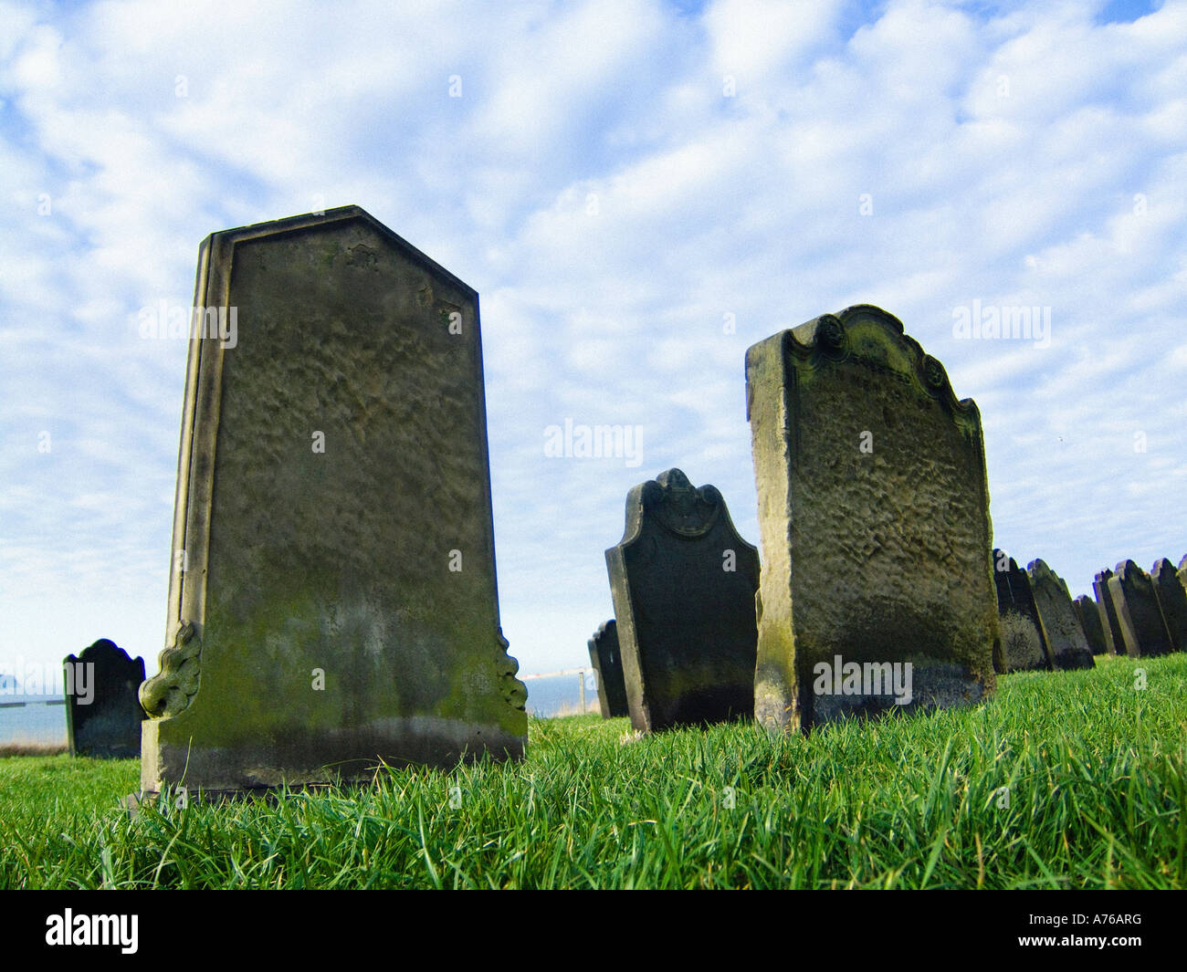 Eroded gravestones shot from a low angle in a churchyard seen against a ...