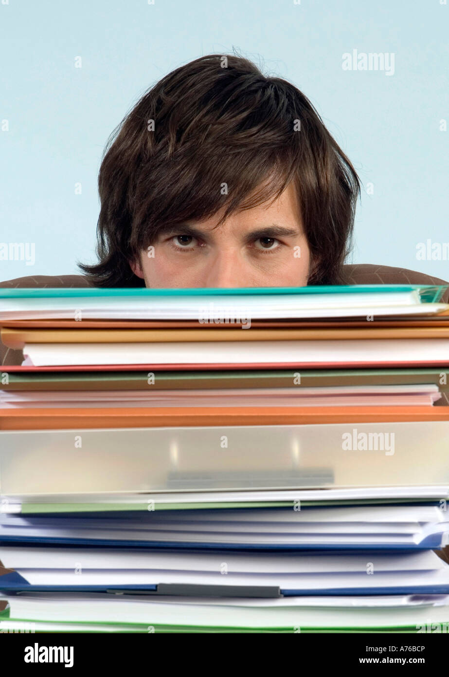 Man sitting on desk with stack of files, portrait, high section, close ...