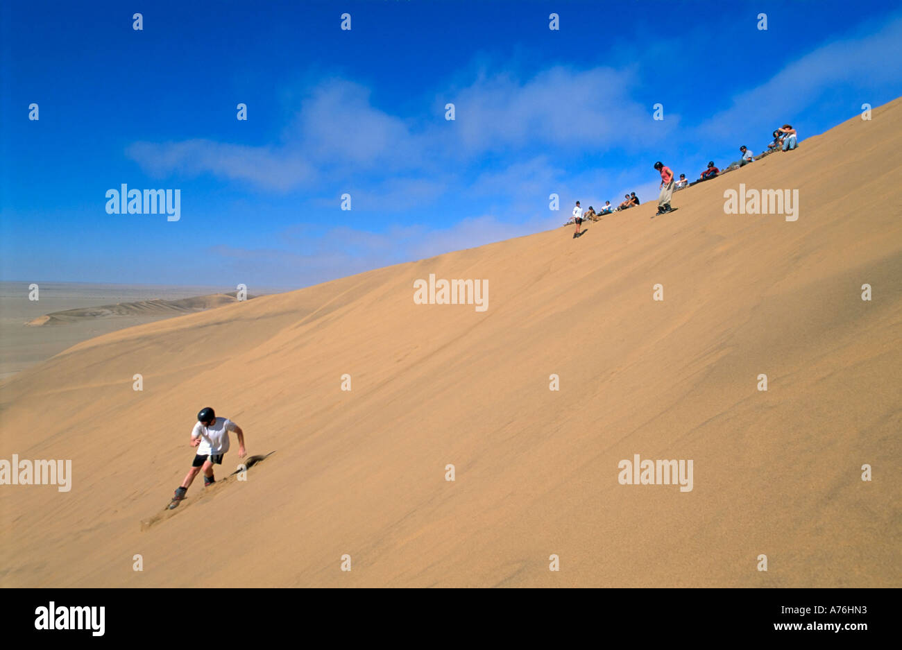 Wide angle of an upright sand boarder surfing down a steep sand dune ...