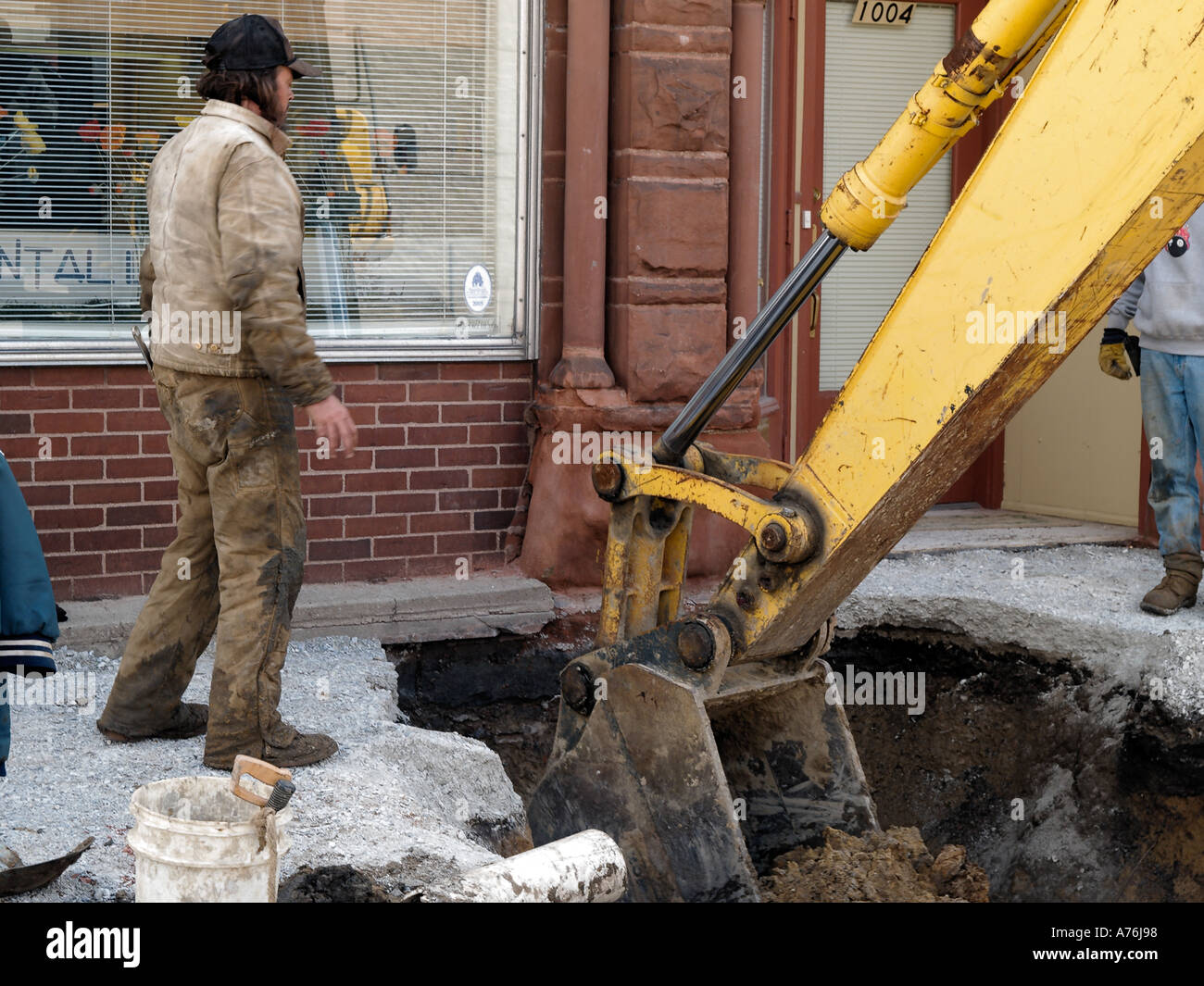 Construction worker stands by as a backhoe digs a trench under the ...