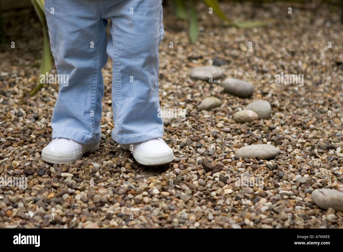 The feet and legs of a child and some large stones on a gravel surface ...