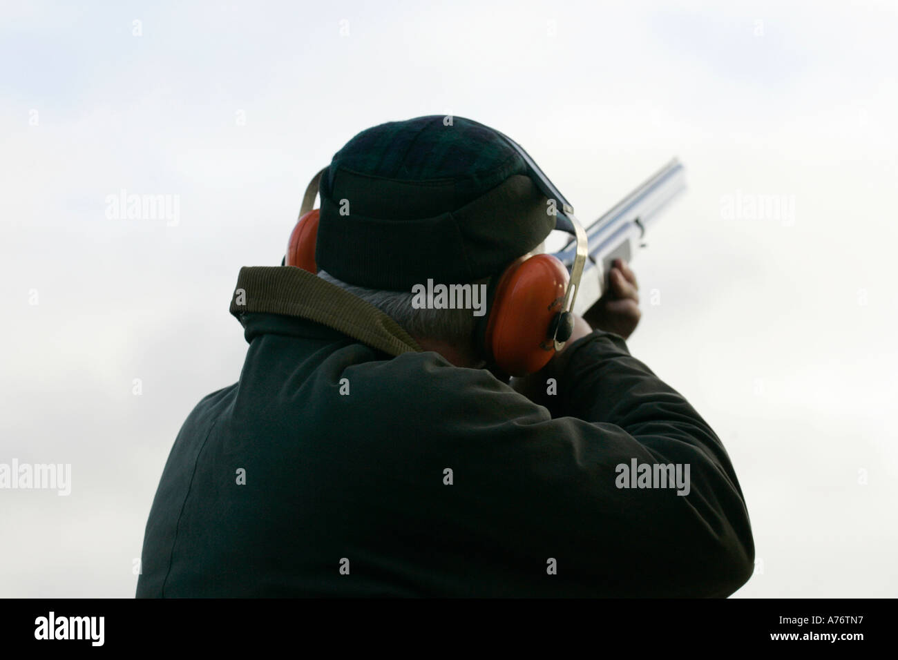 man in cap and orange ear defenders takes aim into sky with shotgun on ...