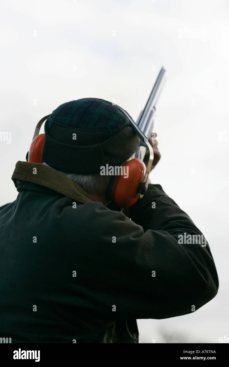 man in cap and orange ear defenders takes aim into sky with shotgun on ...