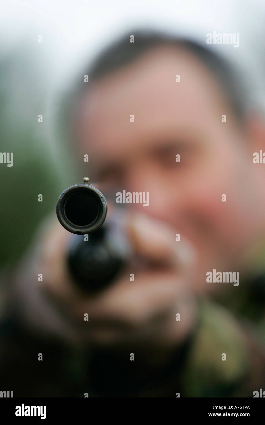 Man in camouflage clothes takes aim at camera with shotgun close up on ...